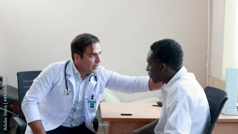 Male orthopedic surgeon examines the shoulders and arms of African man ...