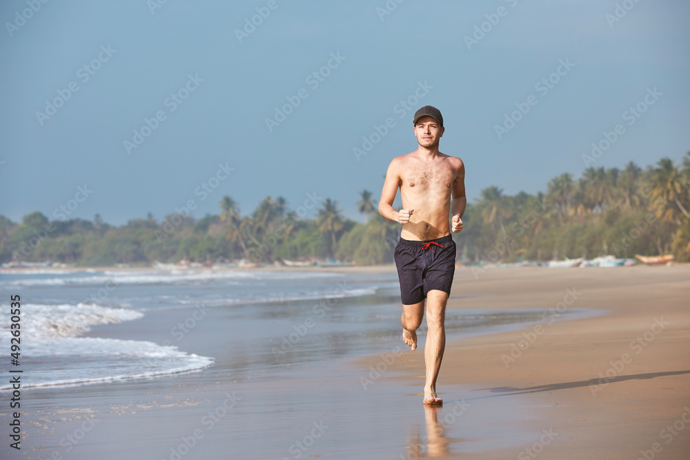 Man running on sand beach in morning light. Front view of barefoot ...