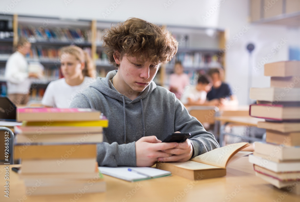 Teenager using mobile phone in the school library Stock Photo | Adobe Stock