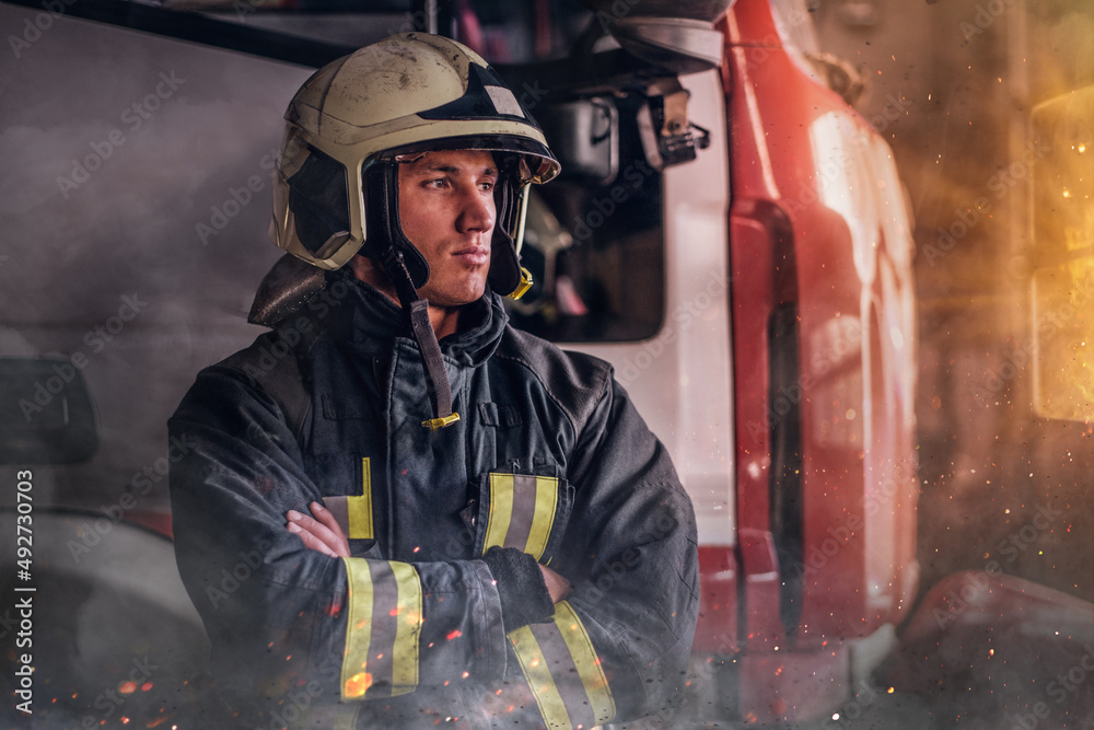 Fireman wearing protective uniform standing next to a fire engine in a ...