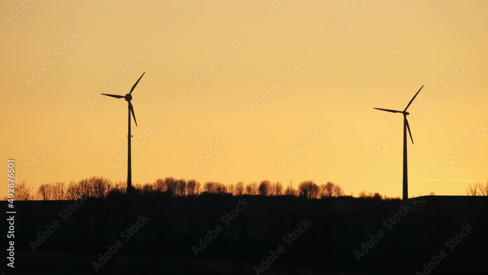 Rotating wind turbine in front of a sunset sky. Telephoto view of green ...