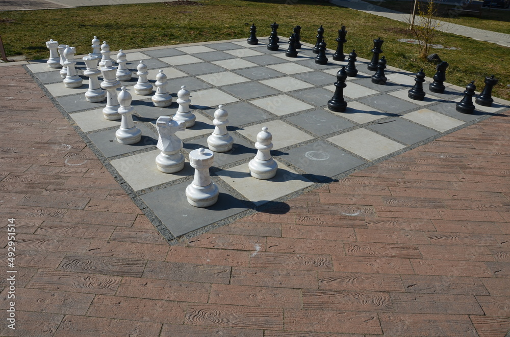 There is a chess area on square with lawn around. chess pieces are made ...