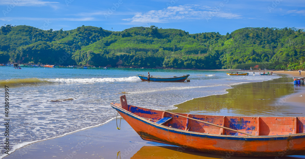 Traditional wooden fishing boats and beautiful hilly beach in East Java ...