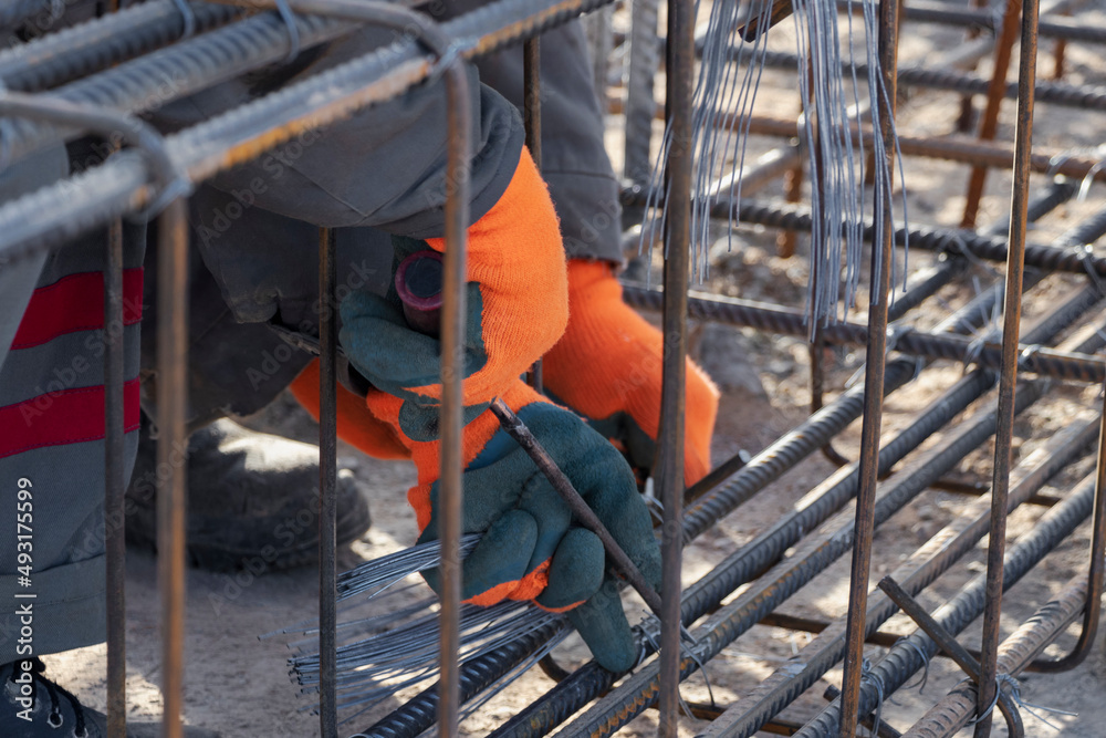 A worker uses steel tying wire to fasten steel rods to reinforcement ...