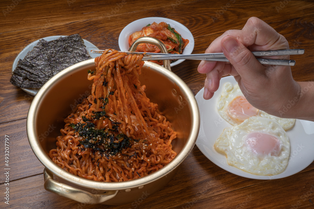 Hand using chopsticks to pick up Ramyeon noodle in a traditional korean ...
