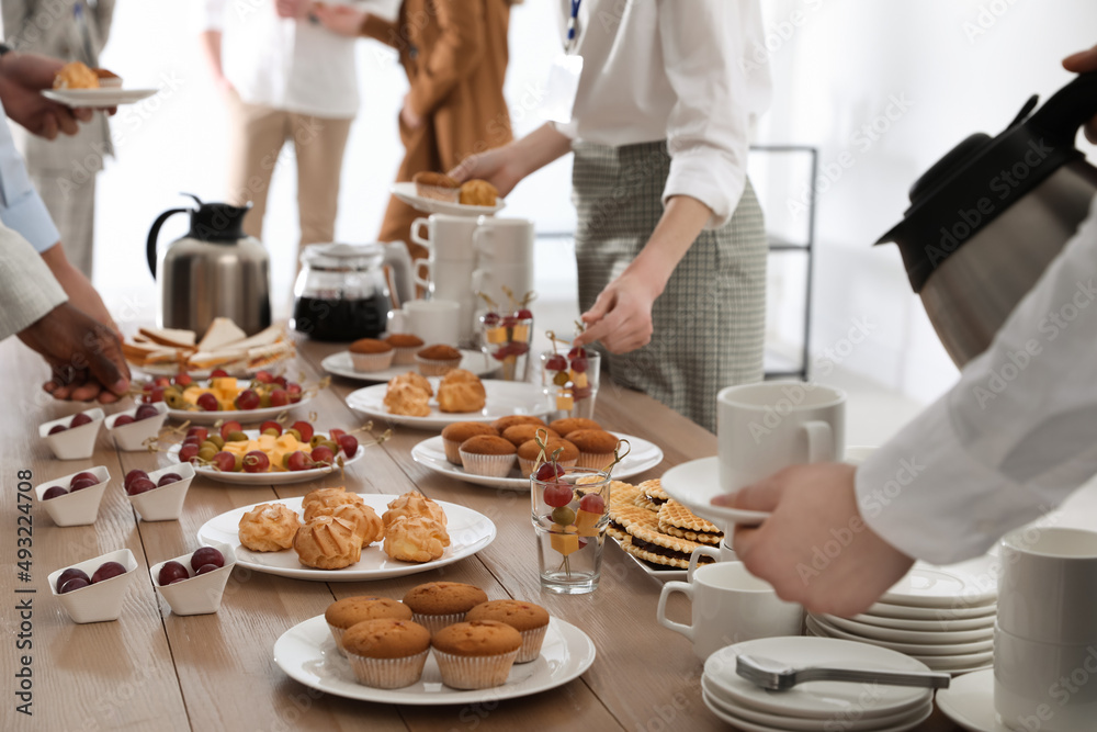 People near table with different delicious snacks during coffee break ...