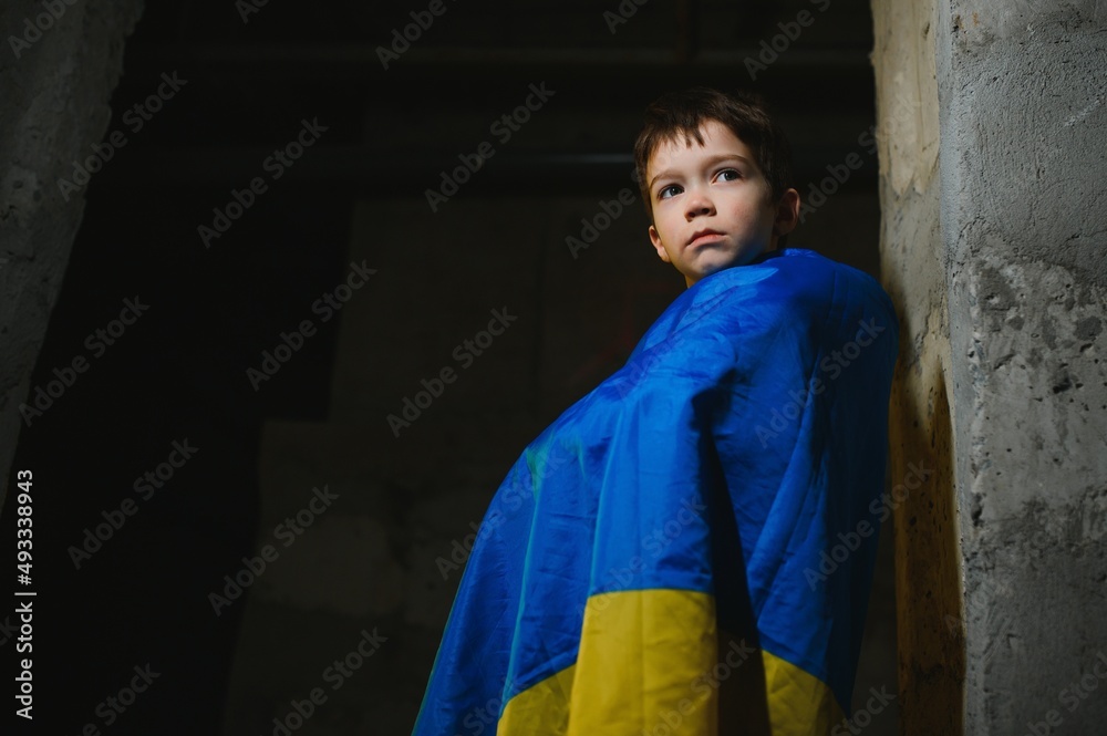 A sad Ukrainian boy wrapped in a Ukrainian flag, hiding from bombings ...