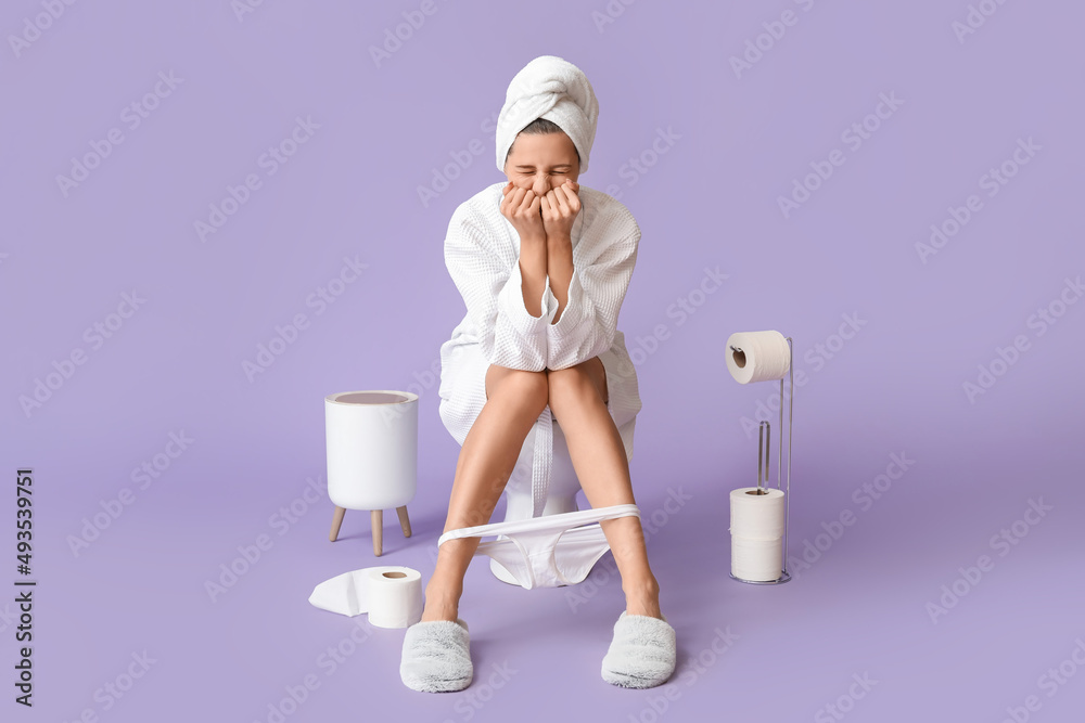 Young woman in bathrobe suffering from diarrhea while sitting on toilet ...