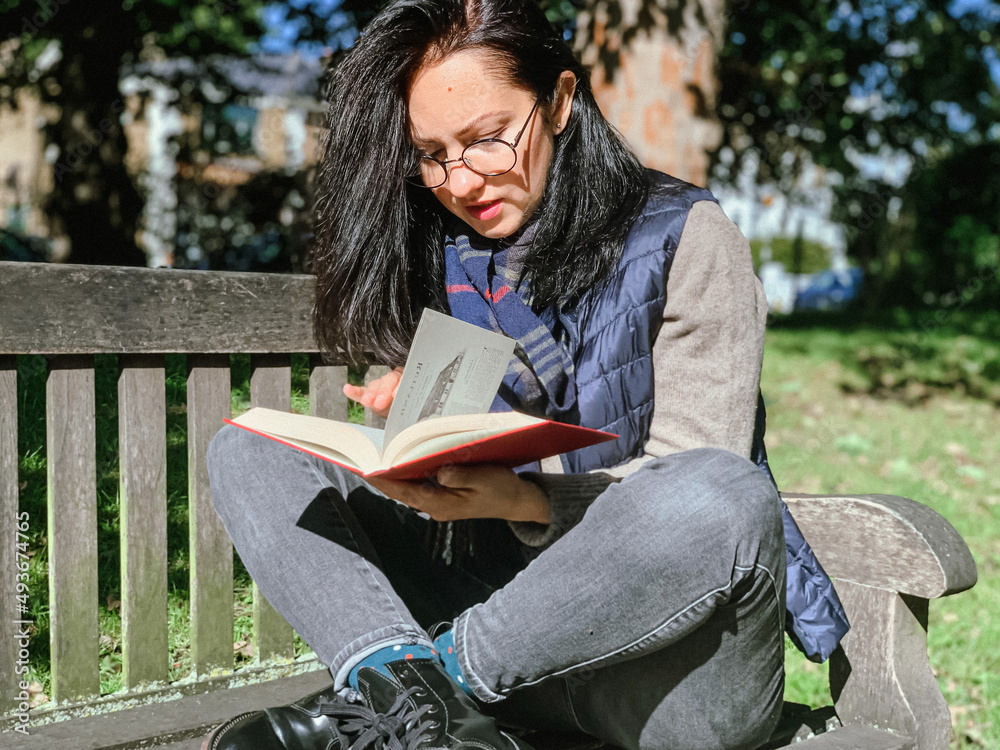 Young woman is reading red book in a park. Young candid millennial ...