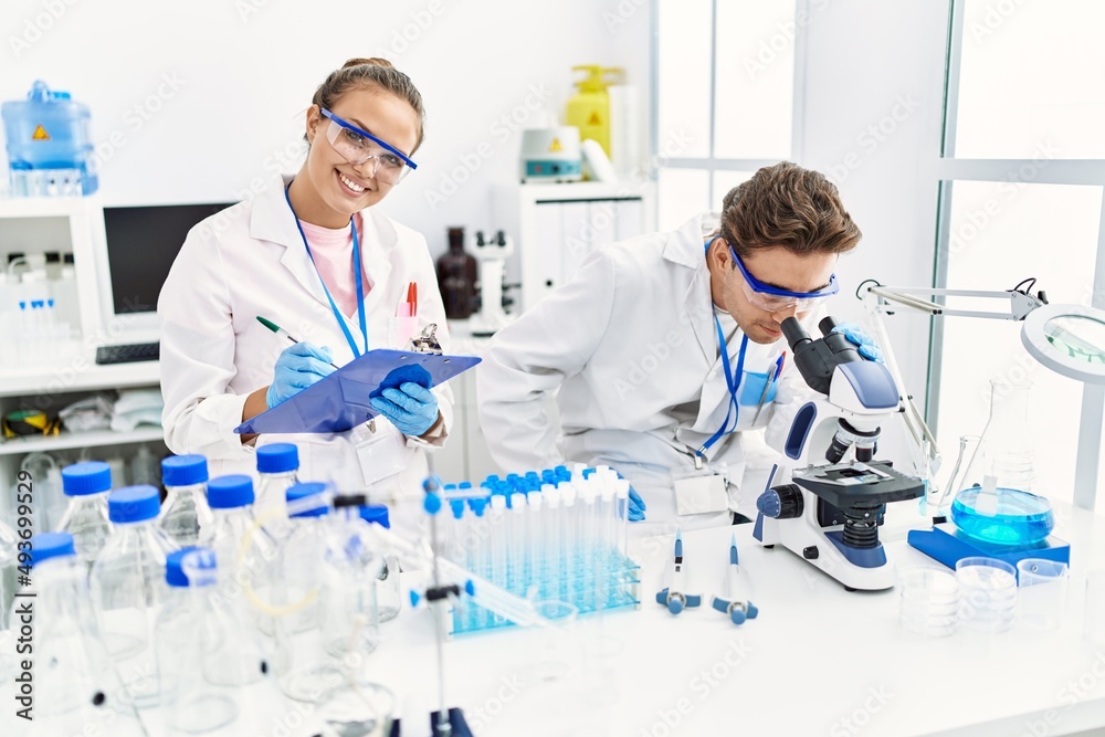Man and woman wearing scientist uniform using microscope write on ...