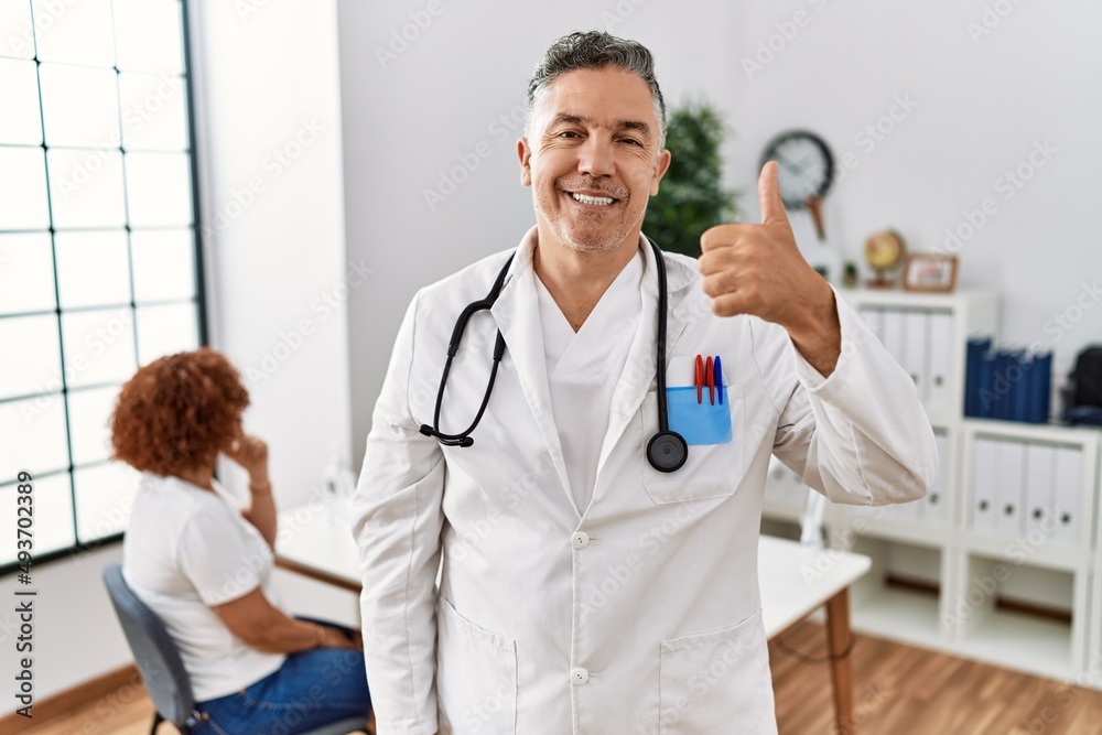 Middle age doctor man at the clinic with a patient doing happy thumbs ...