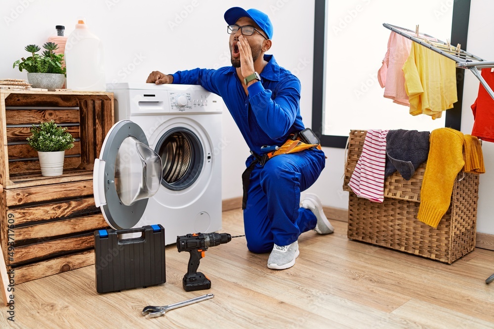 Young indian technician working on washing machine shouting and ...