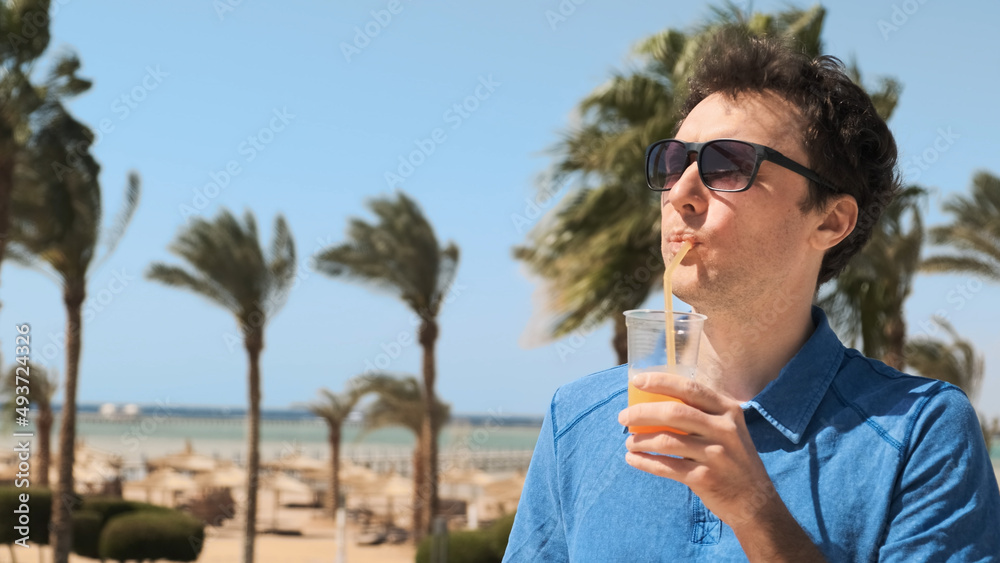 Man on vacation backdrop of palm trees, sea, drinks orange cocktail ...
