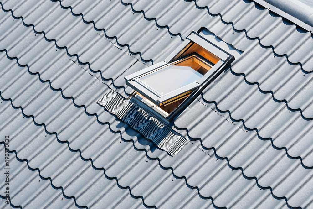 Roof is covered with rows of gray metal tiles. Window skylight ...