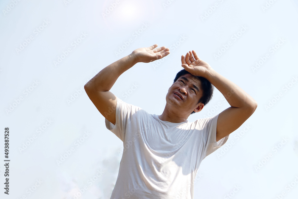 Asian middle-aged man feels hot, stands outdoor in sunny day. Concept ...