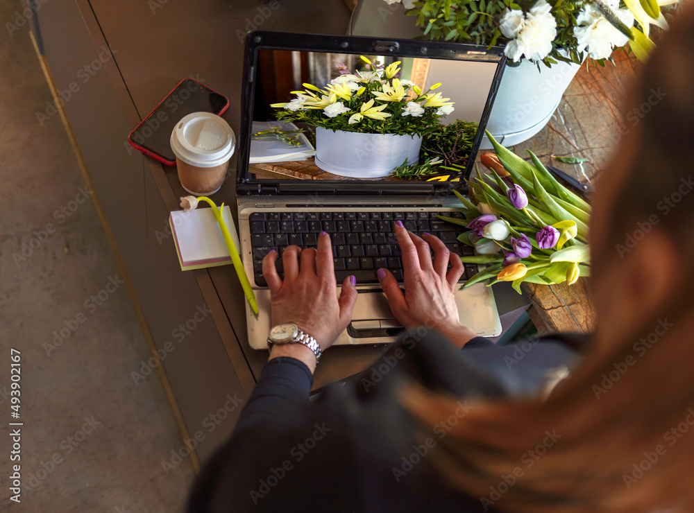 Salesperson in floral shop using laptop and arranging delivery with app ...