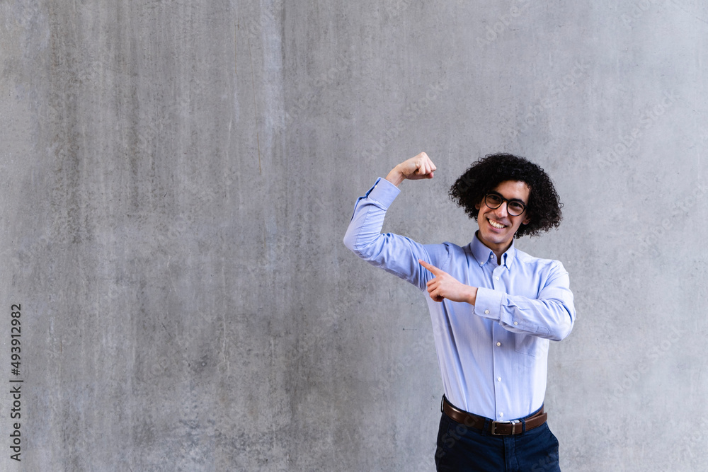 Smiling man flexing muscle standing in front of gray wall Stock Photo ...