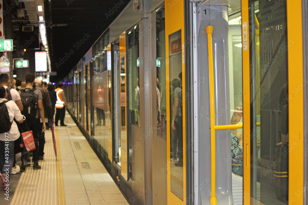 Yellow and grey train with its doors open on a crowded platform in an ...