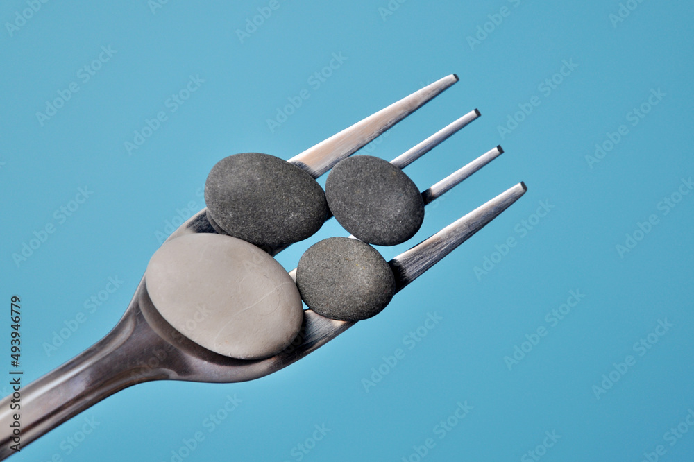 Stones on the fork. A symbol of heavy, unhealthy food. Heaviness in the ...