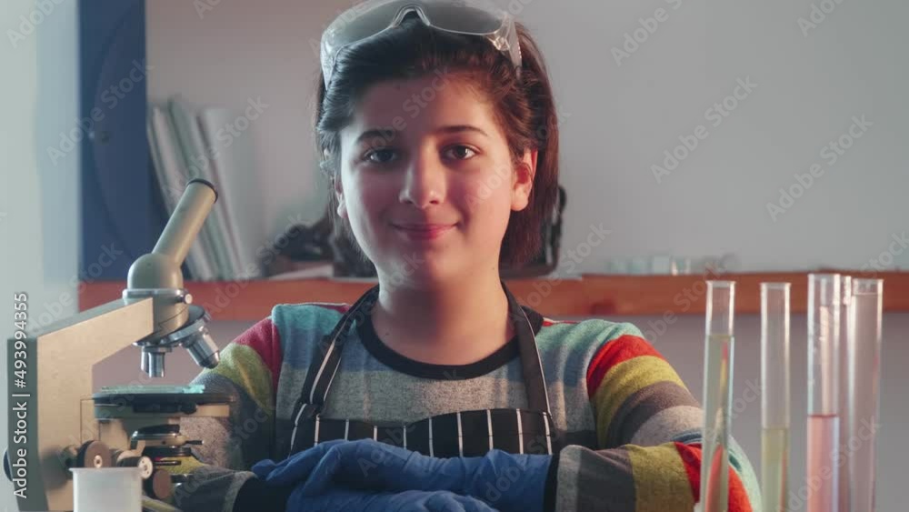A teenager in goggles and gloves in a research home laboratory smiles ...