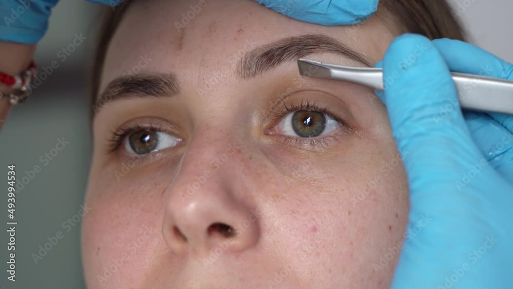 gloved hands pluck the hairs under the eyebrow with tweezers close-up ...