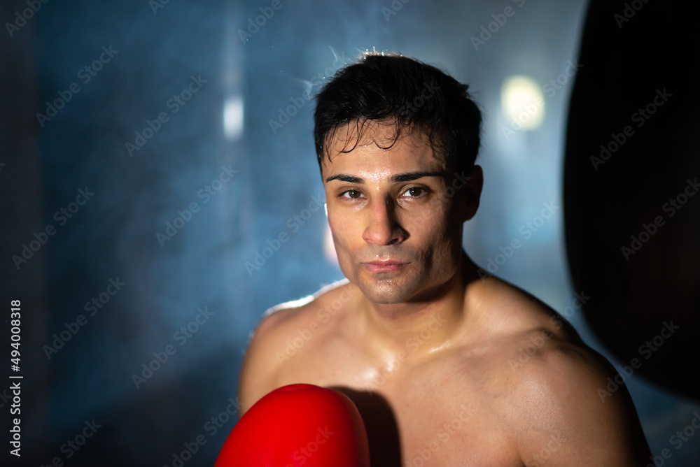 Brunette shirtless boxer in dark gym. Portrait of serious young ...