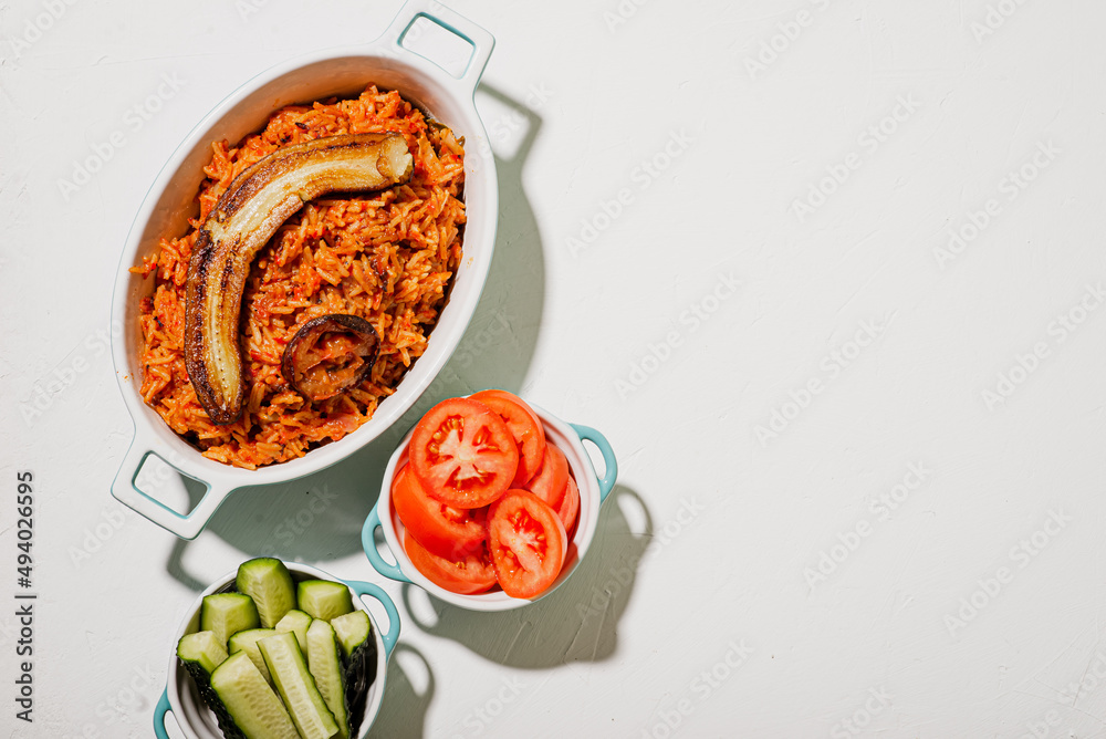 Jollof rice with fried banana. Fresh vegetables - tomato and cucumber ...