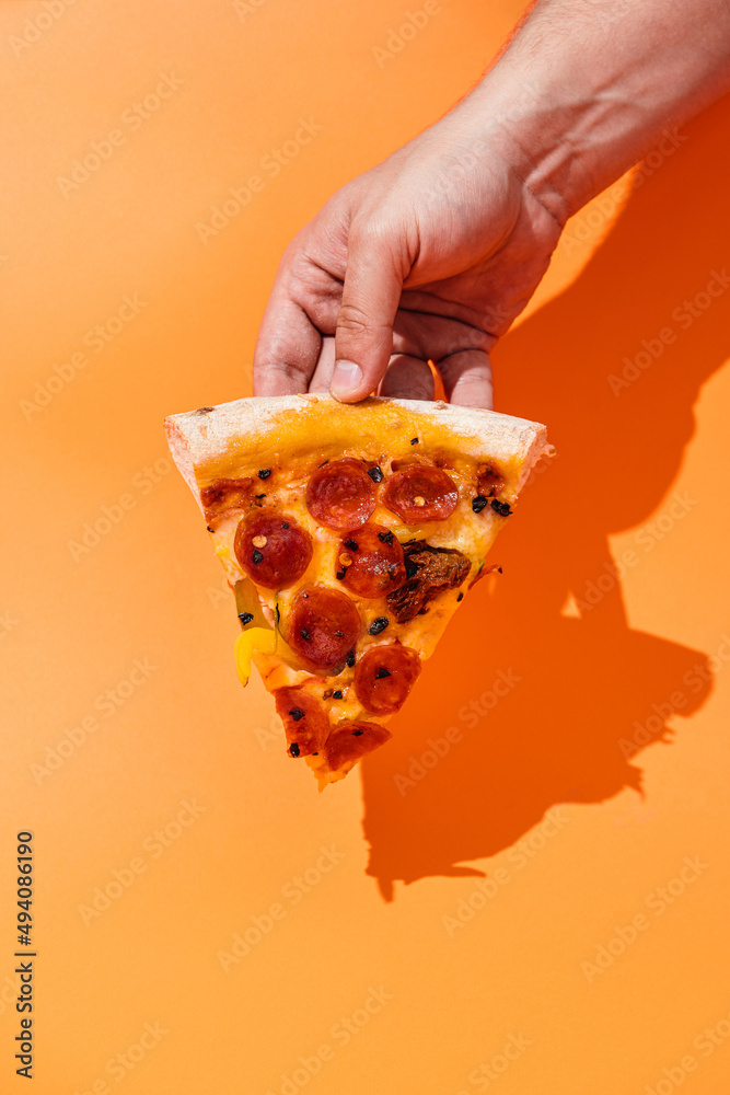 Piece of Pizza in hand with chorizo sausage, sweet peppers, sun dried ...