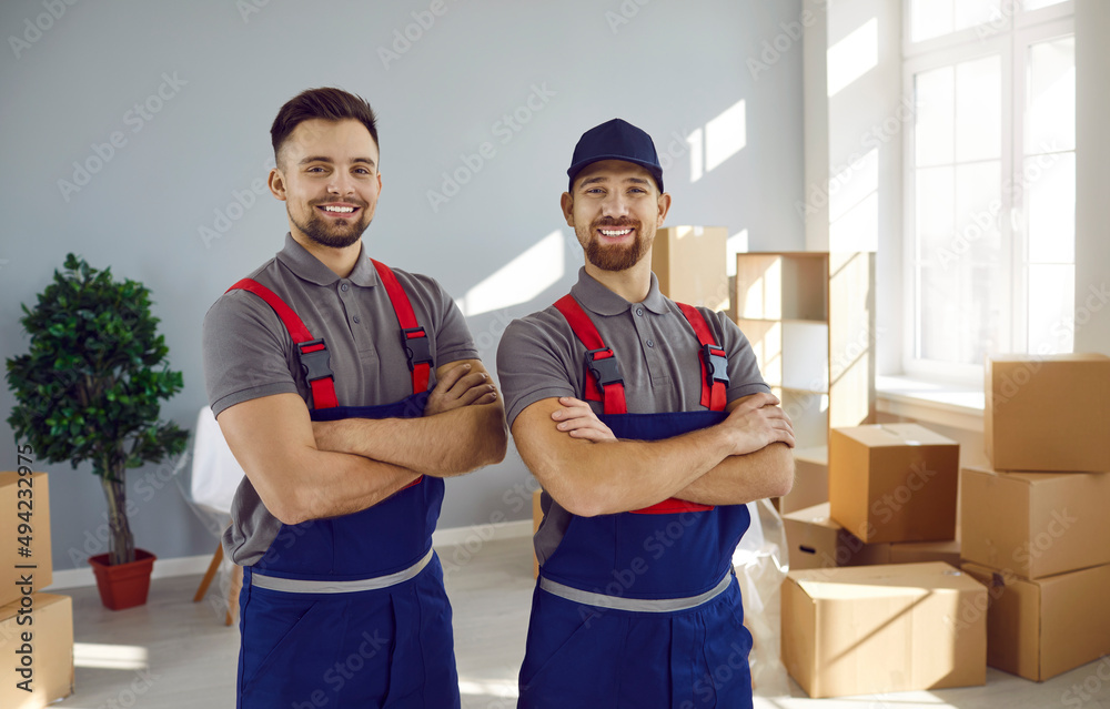 Movers team. Two young cheerful employees of moving service in overalls ...