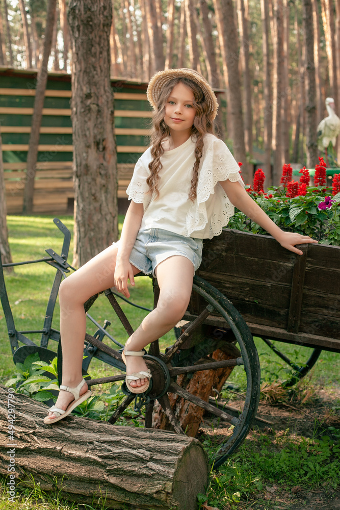 Carefree tween girl sitting on old wooden cart decorated as flowerbed ...
