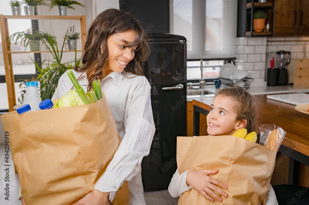 Cheerful little daughter helping the mother to carry groceries from the ...