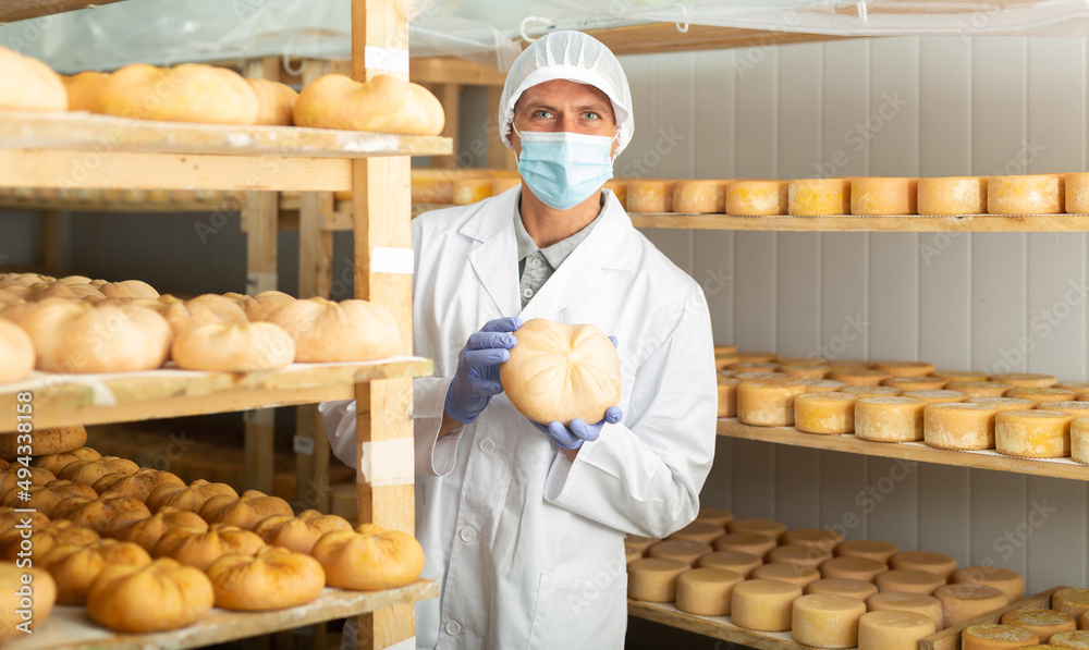 Professional cheese maker in white coat and protective face mask ...