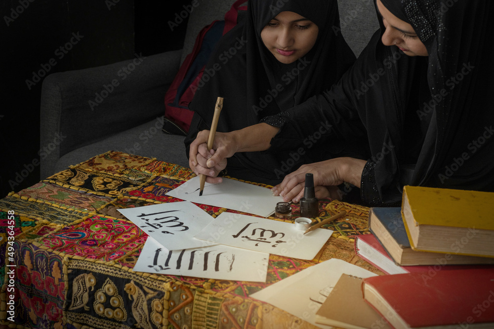 Little Muslim girl and mom wearing black hijab, write Arabic alphabet ...