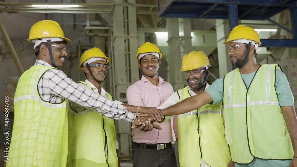 Handheld shot, group of factory workes with engineer joining hands at ...