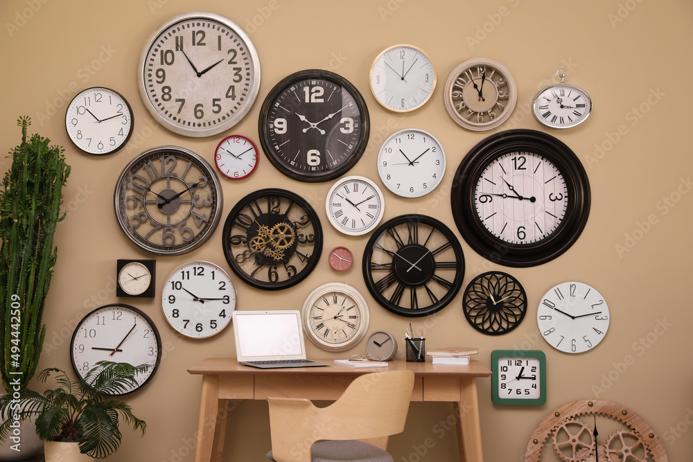 Stylish room interior with collection of wall clocks and workplace ...