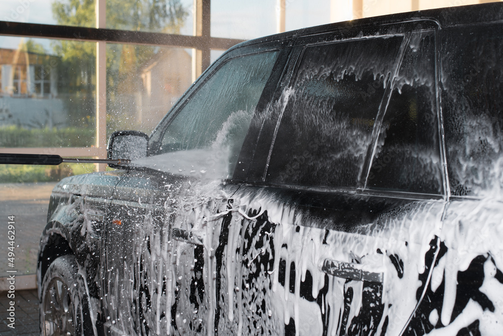 Hand washing a black SUV car with high pressure water pump with foam ...