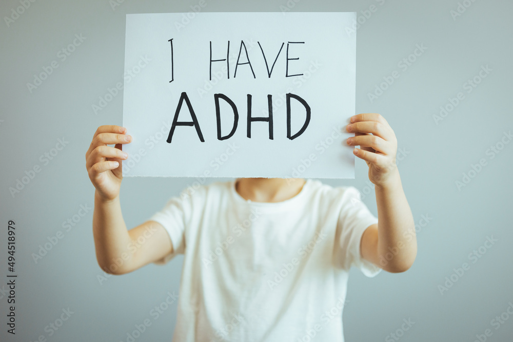 Young boy holds ADHD text written on sheet of paper. ADHD is Attention ...
