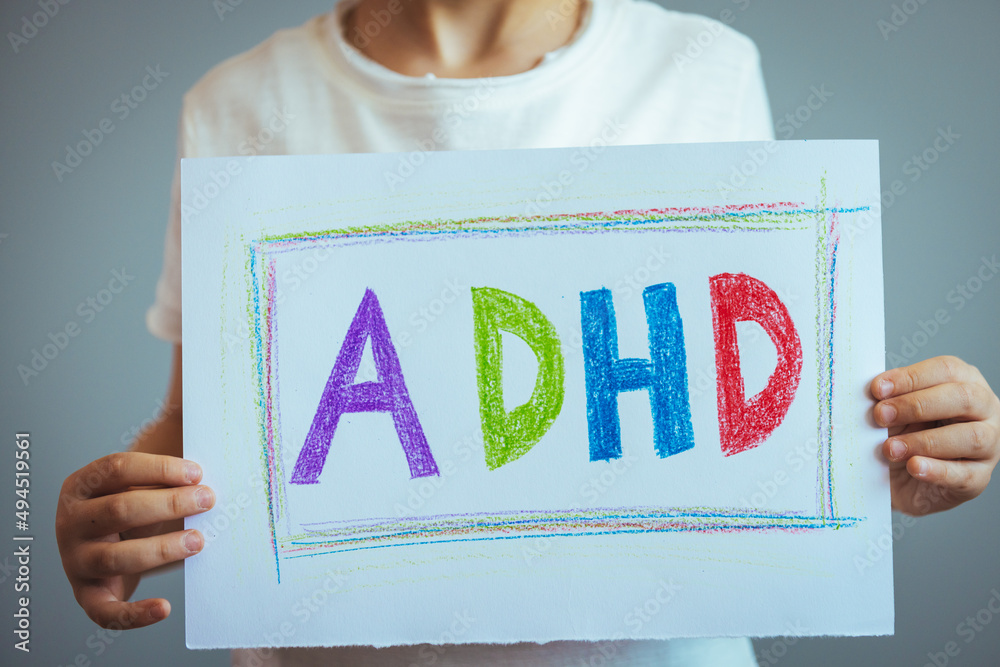 Young boy holds ADHD text written on sheet of paper. ADHD is Attention ...