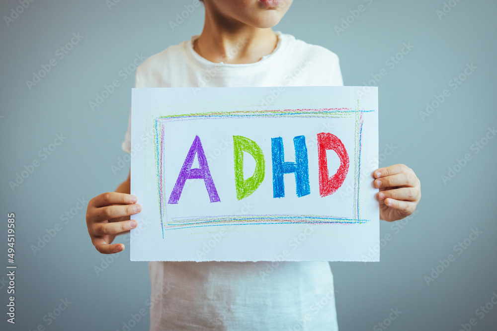 Young boy holds ADHD text written on sheet of paper. ADHD is Attention ...