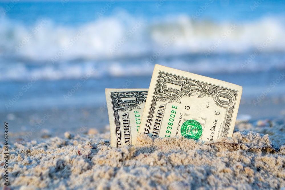 Two one dollar bills half buried in sand on sandy seashore close-up ...