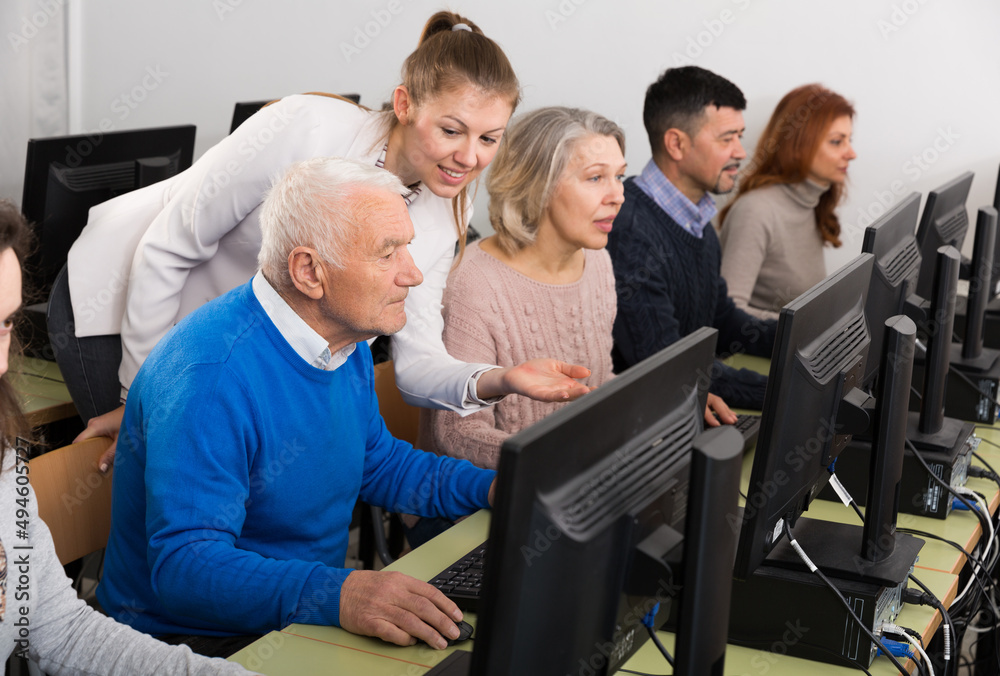 Friendly young female teacher helping mature people to use computer ...