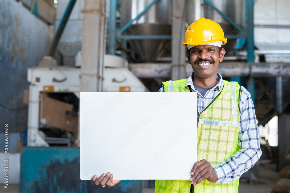 smiling industrial worker with safet hat hosling empty placard or sign ...