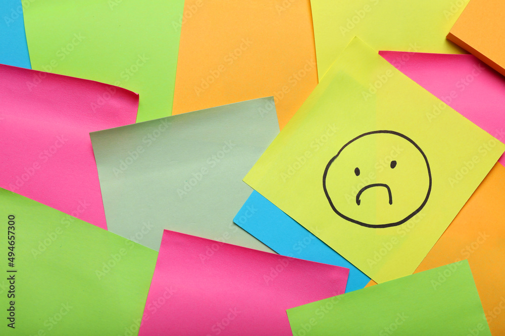 Sticky note with sad face among colorful paper, top view. Space for ...