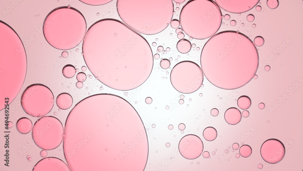 Pink different sized transparent oil drops in clear fluid against pale ...