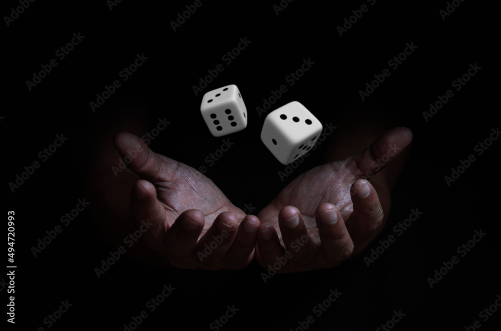 Human hand throwing two white dice in the air on a black background ...