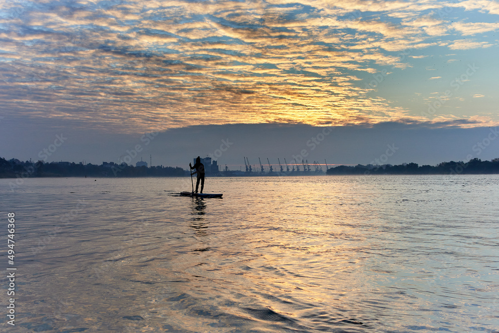 Silhouette of a boy paddle on stand up paddle boarding (SUP) on quiet ...