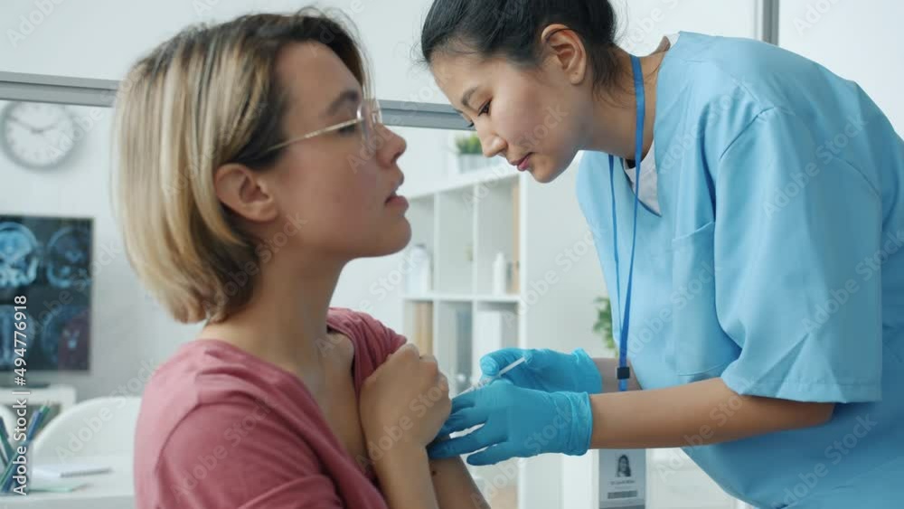 Nurse in uniform giving covid-19 vaccine injection to serious young ...
