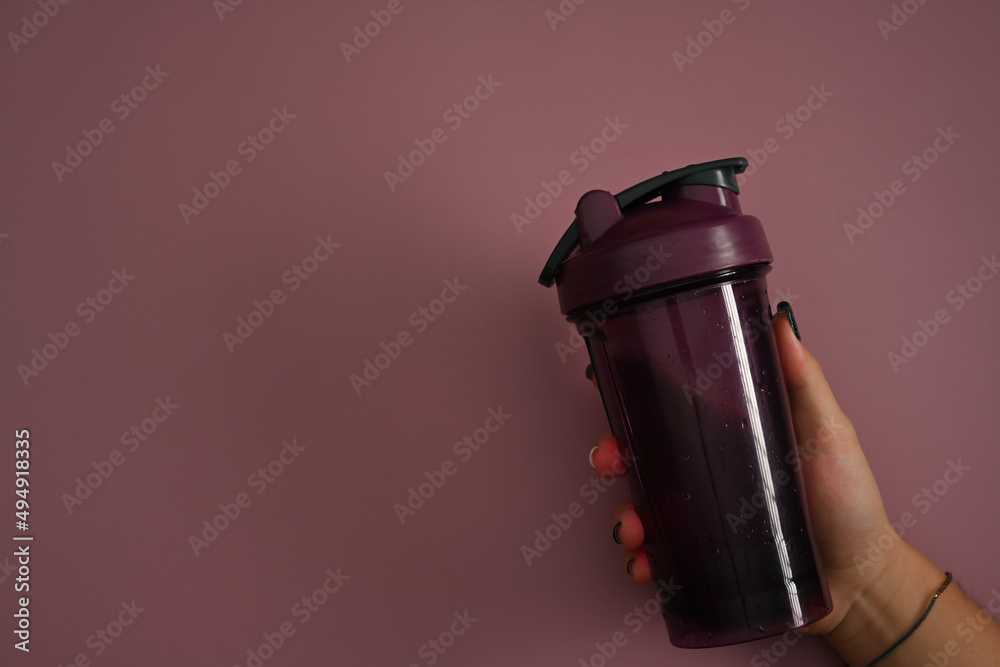 Top view flat lay of hand holding a a protein shaker on a pinky purple ...