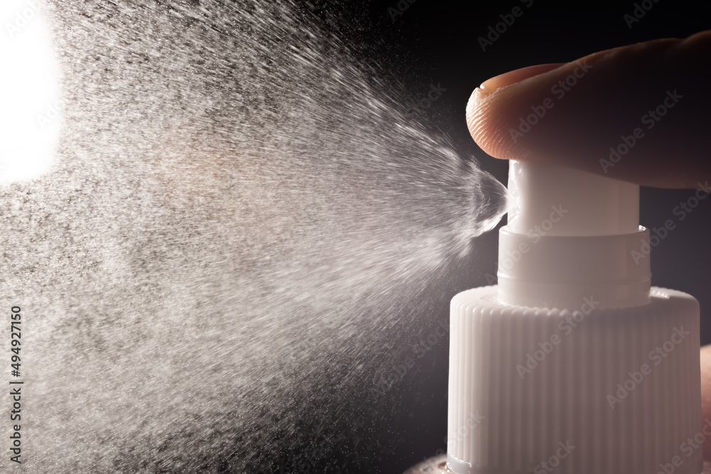 Liquid sprayed from a spray bottle towards a light source. A finger is ...