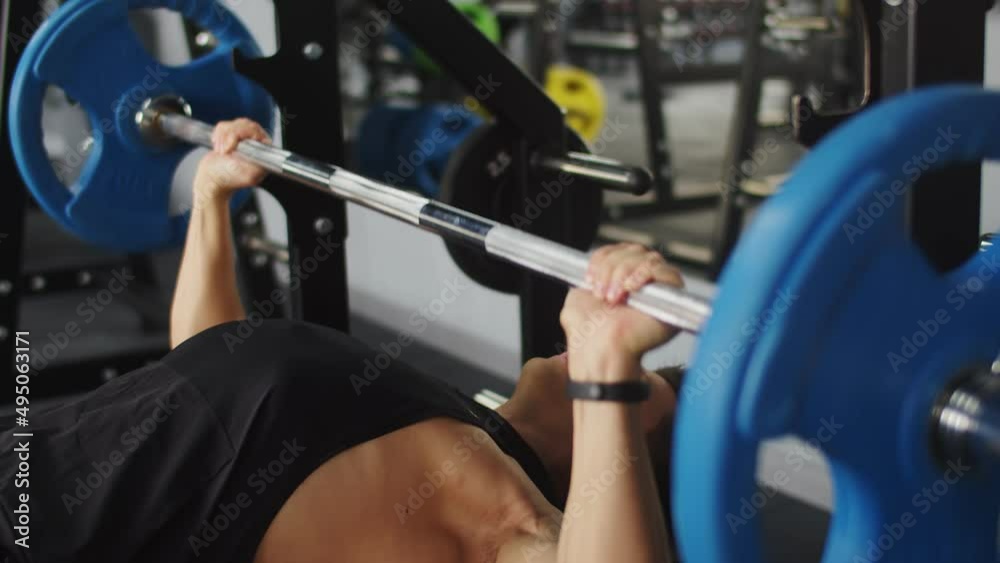 Muscular man trains in gym lifting barbell in prone position, side view ...